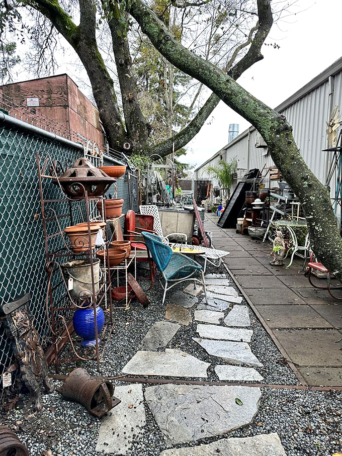 A winding stone path leads through an outdoor vendor area where garden furniture and architectural salvage create a treasure hunter's obstacle course.