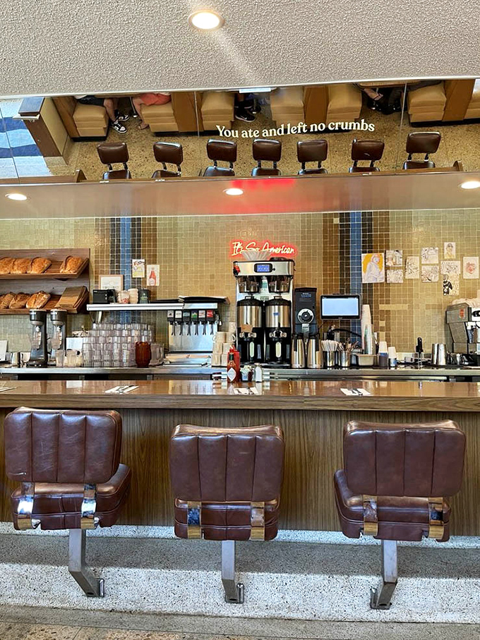 The counter view reveals the diner's beating heart—where coffee machines hum and the mirror reflects the words "You ate and left no crumbs," both challenge and prophecy.