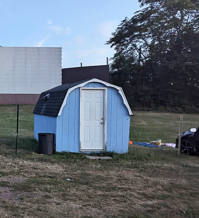 The little blue shed&mdash;humble guardian of equipment, standing sentinel beside the massive screen like a loyal sidekick to a superhero.