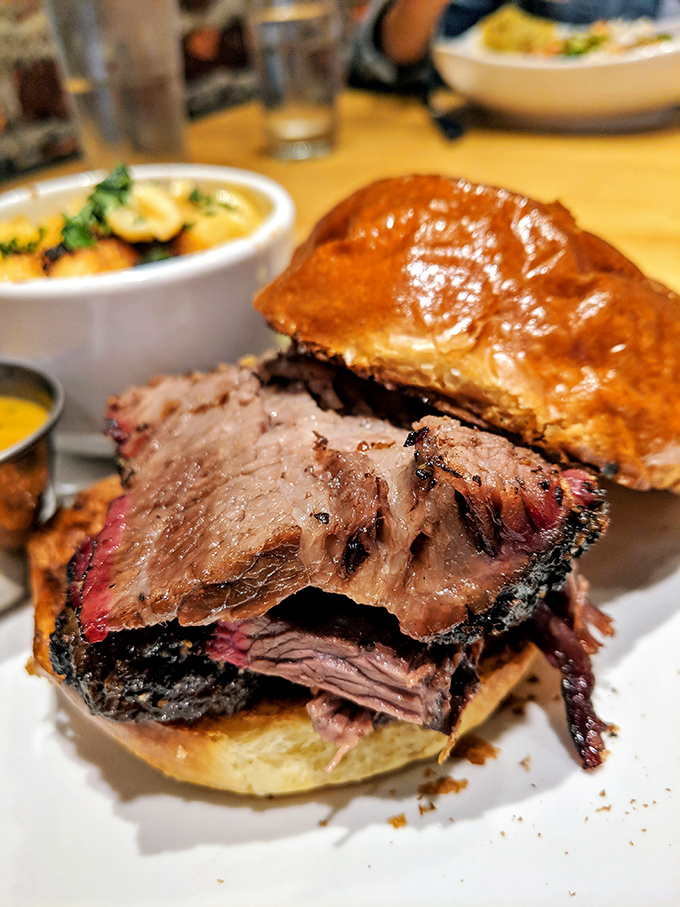 A brisket sandwich that showcases the holy trinity of barbecue perfection: smoke ring, rendered fat, and a bark so beautiful it belongs in an art gallery.