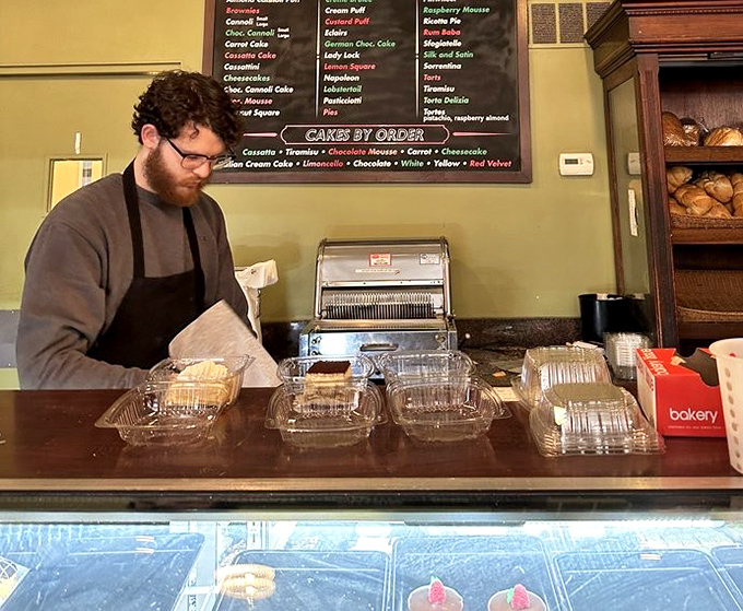 Behind every perfect pastry is a dedicated artisan, carefully packaging edible joy for eager customers. The display case below holds tomorrow's happy memories.