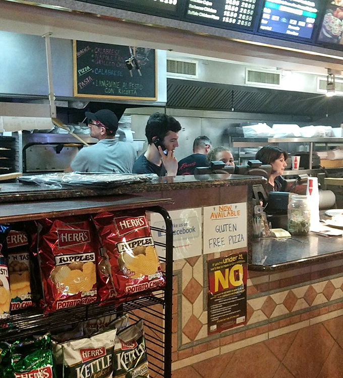 The bustling counter where pizza dreams come true. Watch as orders are called, phones ring, and the organized chaos of a beloved local institution unfolds.