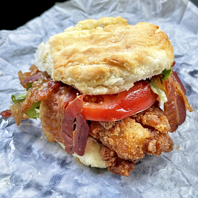 Architecture of deliciousness &ndash; layers of crispy chicken, fresh vegetables, and bacon create a towering biscuit sandwich that requires both hands and dedication.