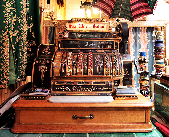 The "Sea Witch Saloon" antique cash register stands as both functional artifact and steampunk sculpture amid vintage textiles.