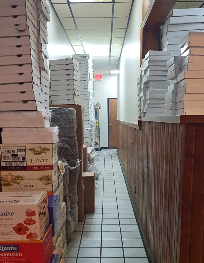 The hallway of pizza boxes stands ready like soldiers awaiting deployment. Each cardboard vessel will soon cradle a circular masterpiece on its journey home.