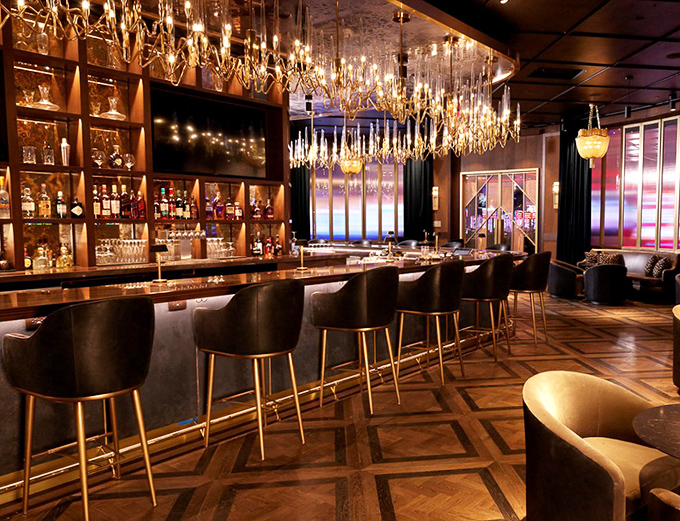 The bar gleams with bottles arranged like a liquid library, each promising stories and memories waiting to be poured.