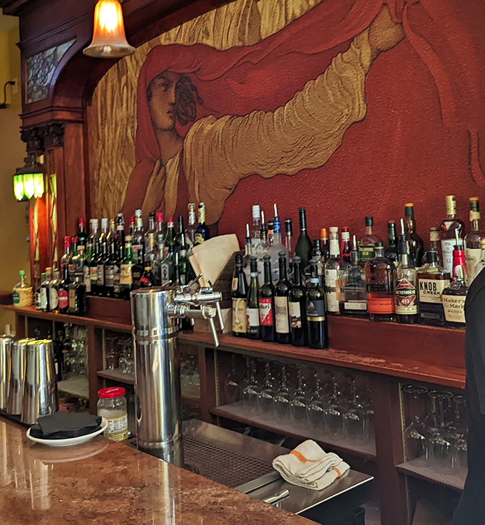 The bar mural watches over bottles like a guardian spirit of libations. Amber lighting transforms even a simple glass of water into something ceremonial.