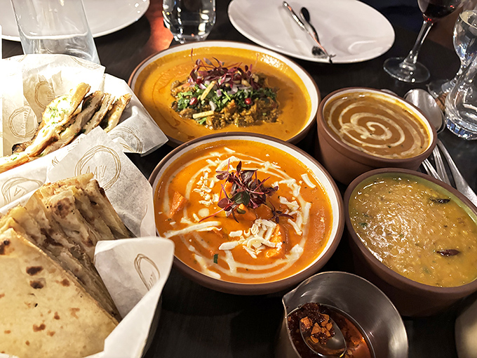 A table transformed into an artist's palette&mdash;golden curries swirled with cream, dal glowing like liquid sunshine, and naan ready to serve as the perfect edible spoon.