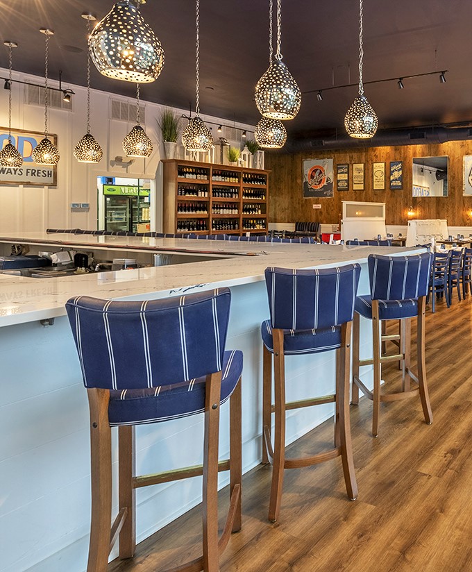 The counter seating offers front-row views of culinary magic. Those pendant lights cast the perfect glow for food that deserves its own spotlight.