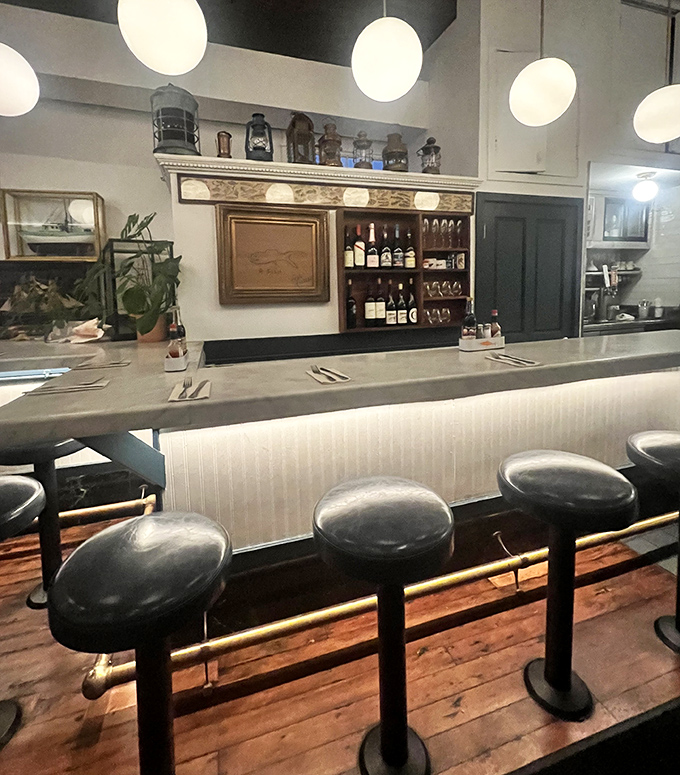 The counter seating offers front-row tickets to the culinary show, where nautical charm meets urban sophistication under the warm glow of pendant lights.