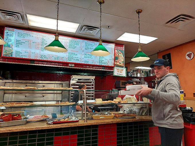 The green pendant lights cast a warm glow over the counter, where pizza magic happens before your eyes in a choreographed culinary dance.