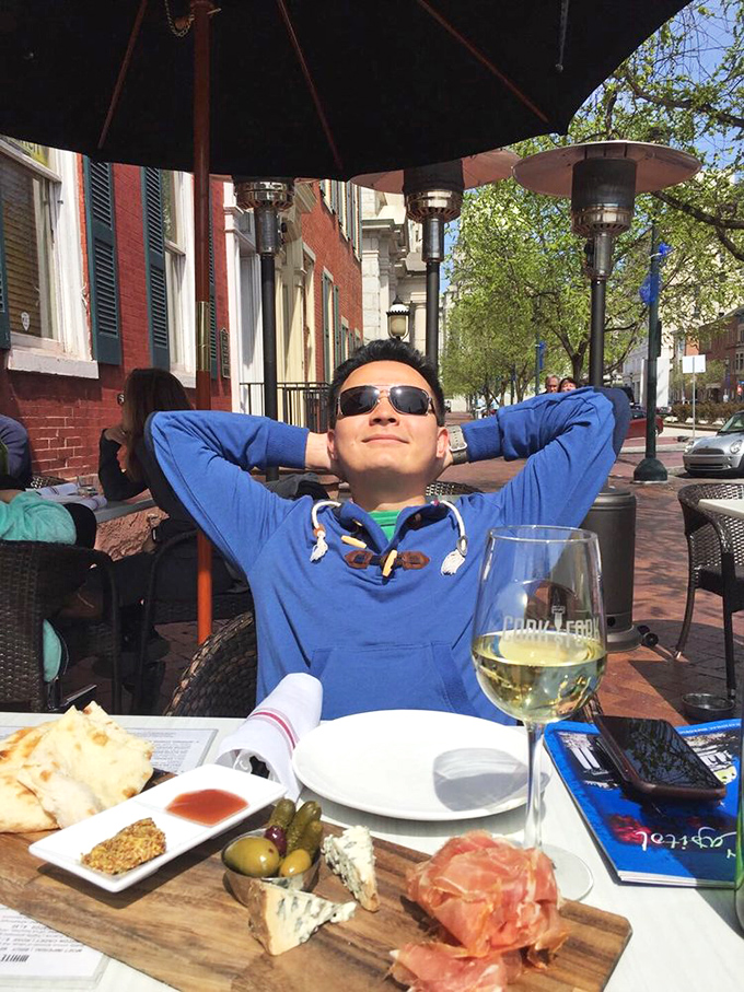 A patron enjoying the perfect trifecta &ndash; sunshine, wine, and a charcuterie board that would make any Italian grandmother nod in approval.