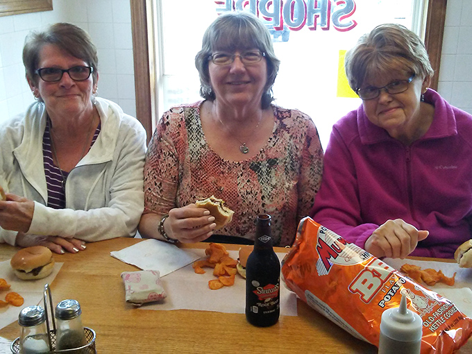 Three friends sharing smiles, burgers, and chips&mdash;the universal language of good food bringing people together since forever.