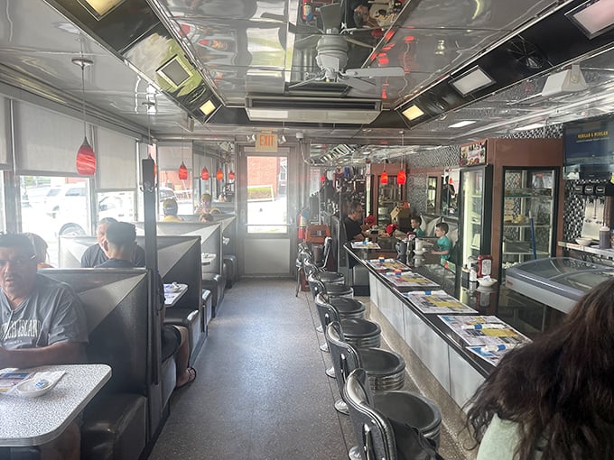The classic diner layout: booths on one side, counter on the other, and conversations bouncing off that chrome ceiling like pinballs.