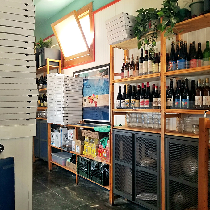 Behind the scenes, stacked pizza boxes await their destiny while wine bottles stand at attention like delicious soldiers.