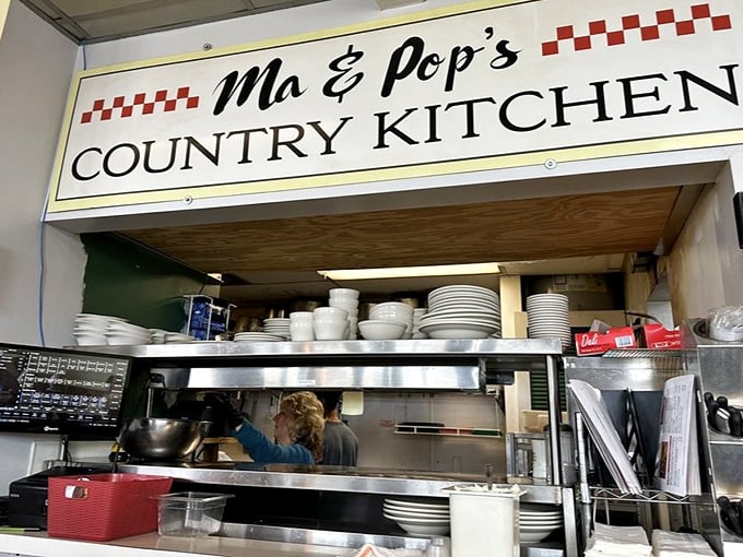 The pass-through window: where kitchen magic becomes plate reality under the watchful eye of the Ma & Pop's sign.