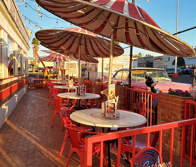 Outdoor seating under candy-striped umbrellas captures desert evenings perfectly. Red metal chairs invite you to linger as the Arizona sun sets.
