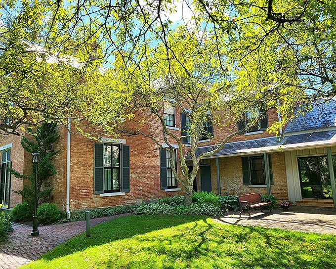 The Castle's exterior basks in dappled sunlight through spring foliage. Brick, bench, and blooms create a peaceful corner for contemplation.