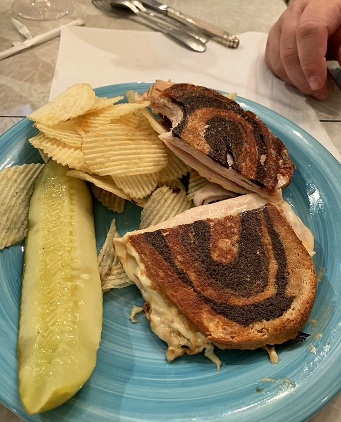 A perfectly grilled sandwich with the telltale marks of a panini press, accompanied by rippled chips and a pickle &ndash; comfort food that transcends time.