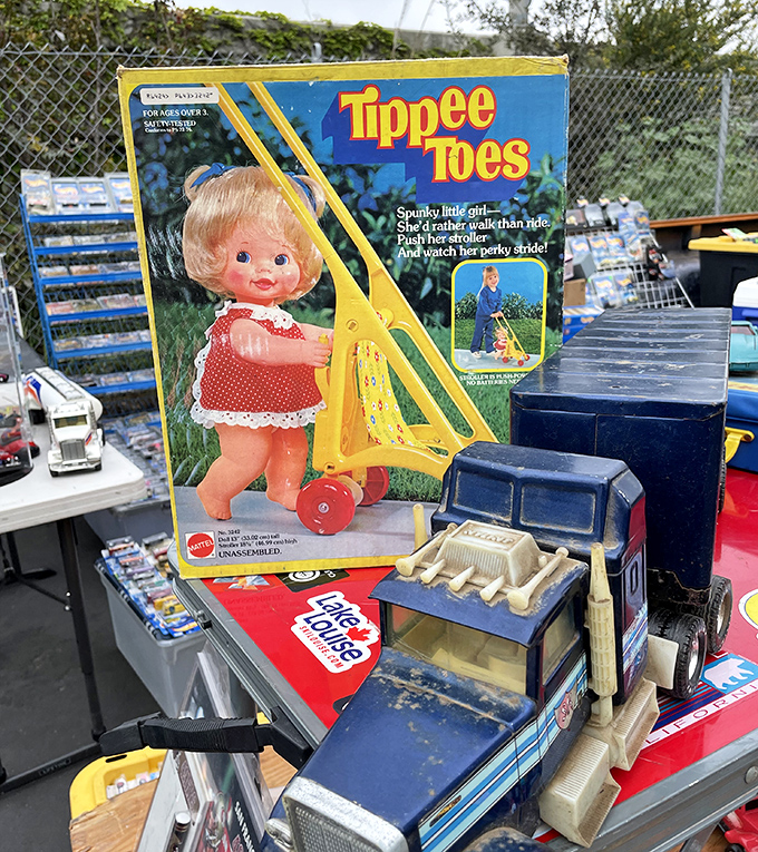 Childhood nostalgia, boxed and ready! This vintage Tippee Toes doll stands guard over toy trucks, a time capsule of playtimes past waiting for new adventures.