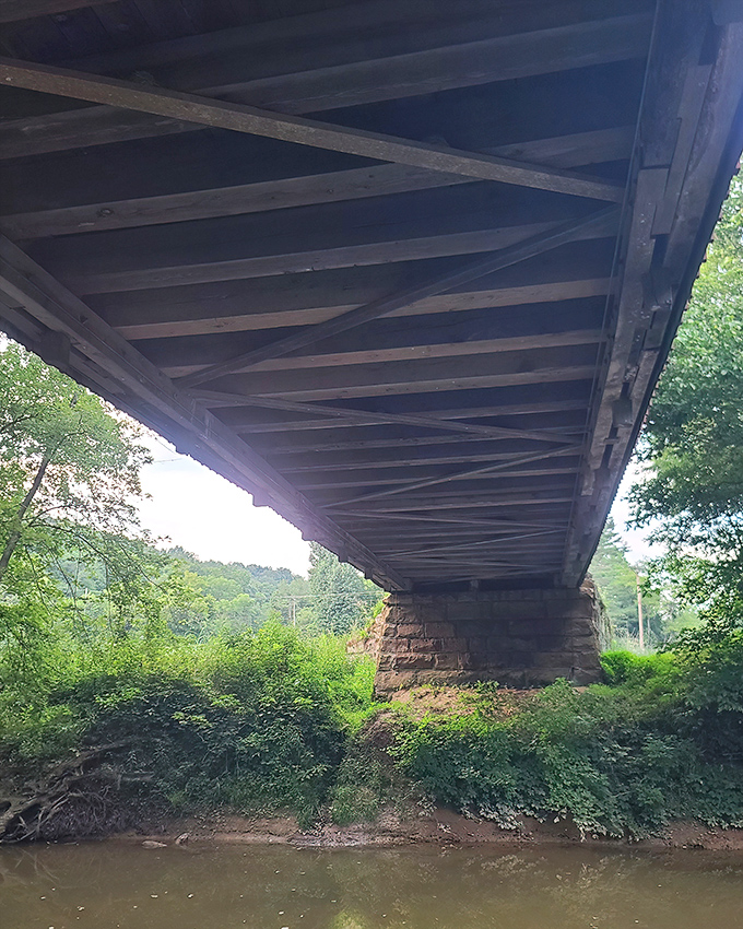 From below, the bridge reveals its sturdy foundation, stone pillars anchoring history firmly against the creek's persistent flow.