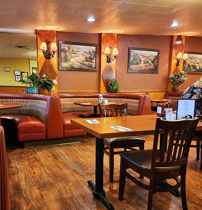 Curved booths and warm lighting create cozy conversation nooks where Thomas Kinkade landscapes on the walls remind you that comfort never goes out of style.