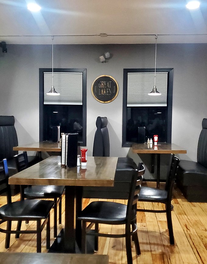 Simple wooden tables beneath pendant lights create dining zones that feel both connected to the energy yet private enough for good conversation.