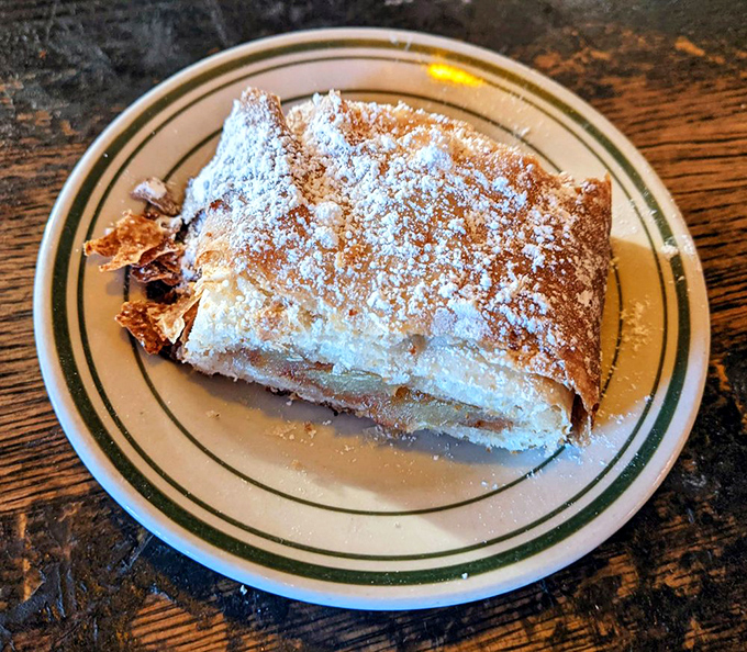 Apple strudel dusted with powdered sugar&mdash;the kind of dessert that makes you push through fullness because missing it would be a culinary crime.