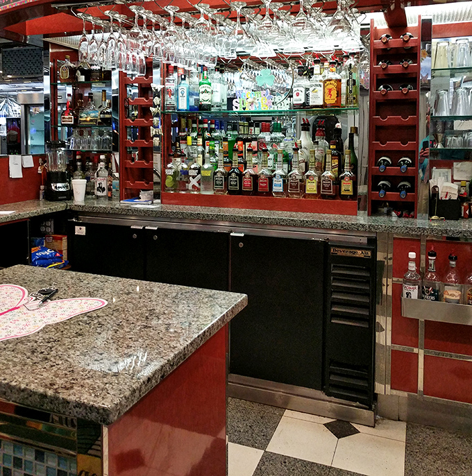 The bar area proves that diners have evolved beyond coffee and milkshakes. Those hanging glasses promise sophisticated sipping alongside your comfort food.