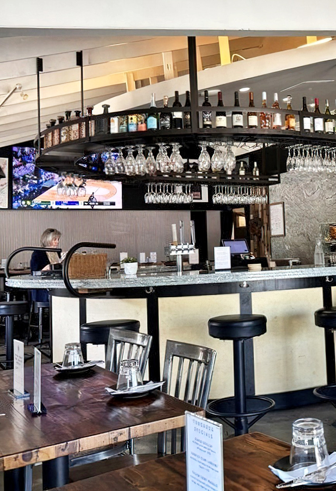 The circular bar where wine glasses hang like crystal stalactites – perfect for solo diners or couples waiting for their seafood feast.