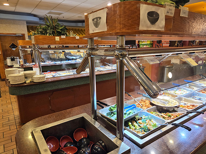 The buffet stations stand ready like culinary islands, each offering its own temptations under the watchful gaze of sneeze guards and serving spoons.