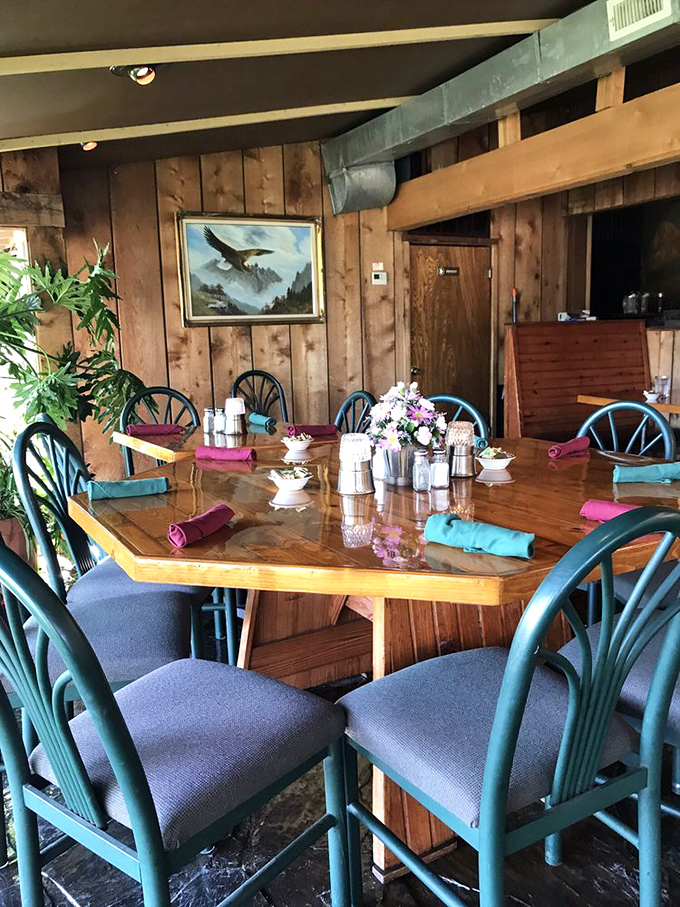 Teal chairs pop against wooden walls adorned with Ozark-inspired art. This table has hosted countless celebrations, confessions, and proposals.