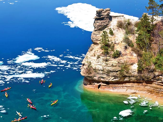 Kayakers explore the base of towering cliffs where Lake Superior's waters shift between emerald and sapphire like a mood ring.