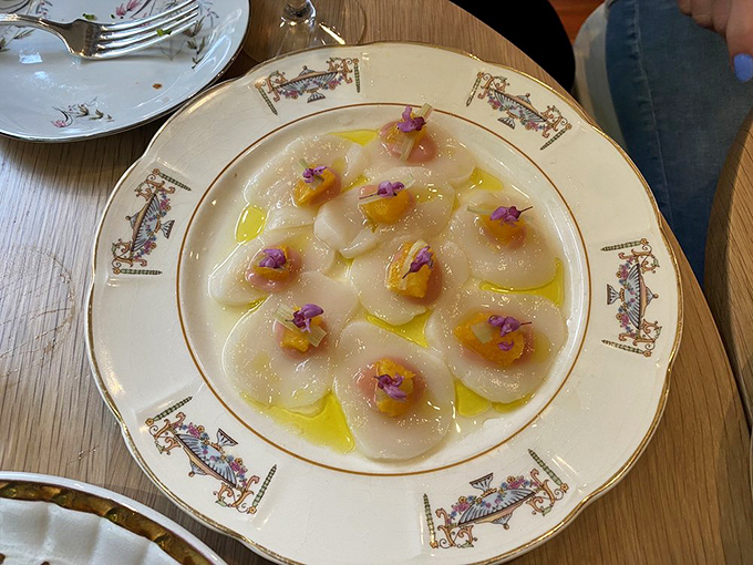 Translucent scallop crudo arranged like petals, adorned with tiny flowers and bathed in olive oil's liquid sunshine.