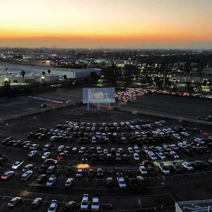 From above, the drive-in transforms into a constellation of headlights and taillights, all oriented toward a single glowing rectangle.