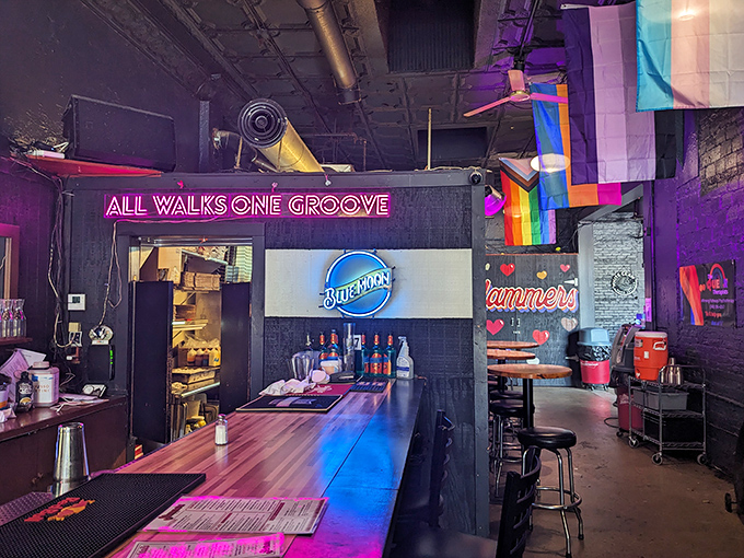 The neon "ALL WALKS ONE GROOVE" sign illuminates the bar area, a glowing manifesto for this inclusive Columbus gathering spot.
