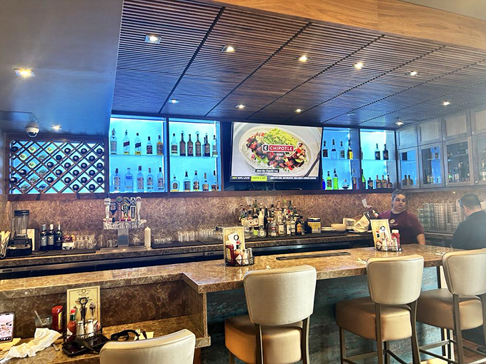 The bar area glows with blue-lit promise, where breakfast and cocktails can coexist in harmony like the best kind of blended family.