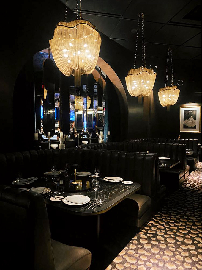 Curved booths create intimate universes where conversations flow as smoothly as the wine, under cascading jellyfish-like chandeliers.