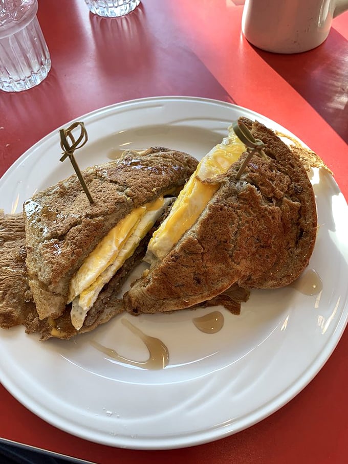 Breakfast sandwich perfection: egg and cheese nestled between hearty bread slices, with maple syrup nearby for those brave enough to create a sweet-savory masterpiece.