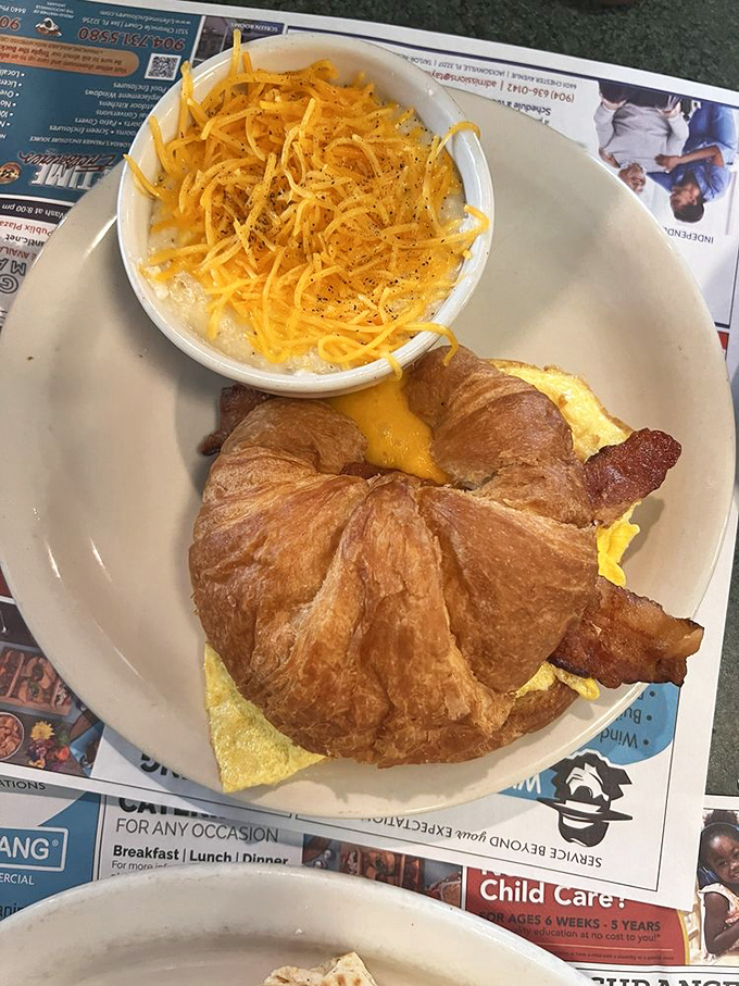 Breakfast sandwich architecture at its finest &ndash; a golden croissant cradling eggs, bacon and cheese with a side of cheesy grits for good measure.