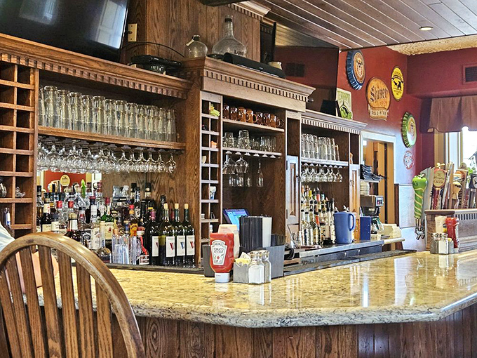 The bar stands ready for service like a liquid library, where bottles line up with military precision under the watchful gaze of vintage beer signs.