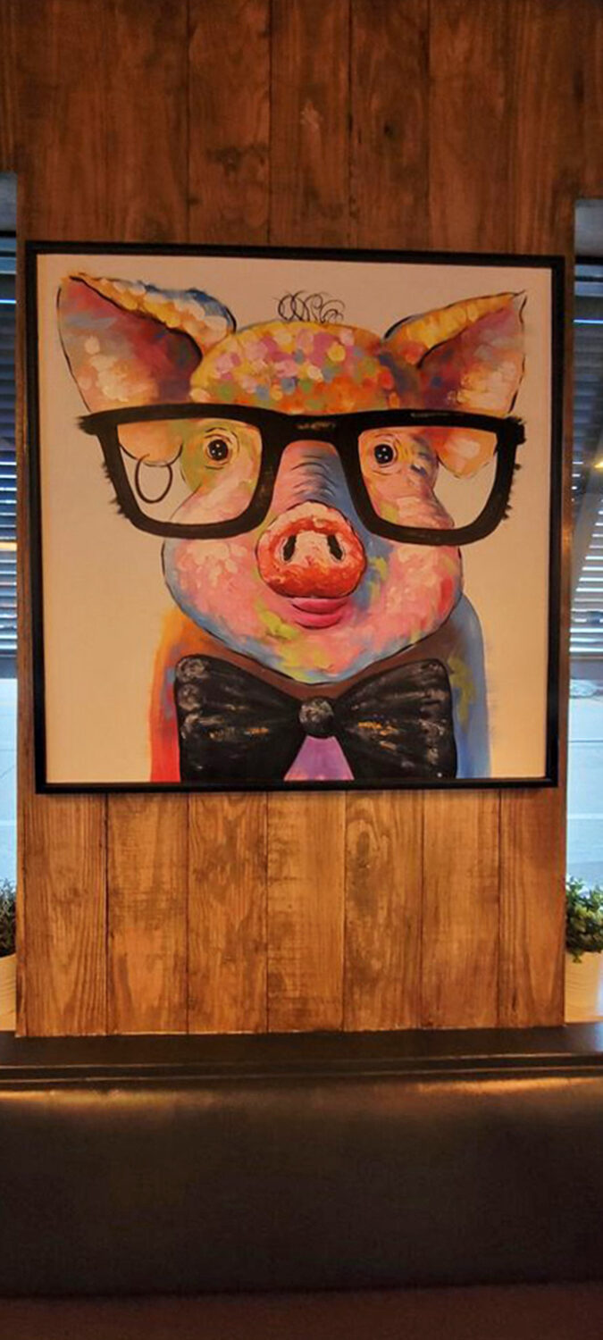 A bespectacled pig in a bow tie watches over diners like the spirit animal of sophisticated barbecue. Whimsy and wisdom in porcine form.