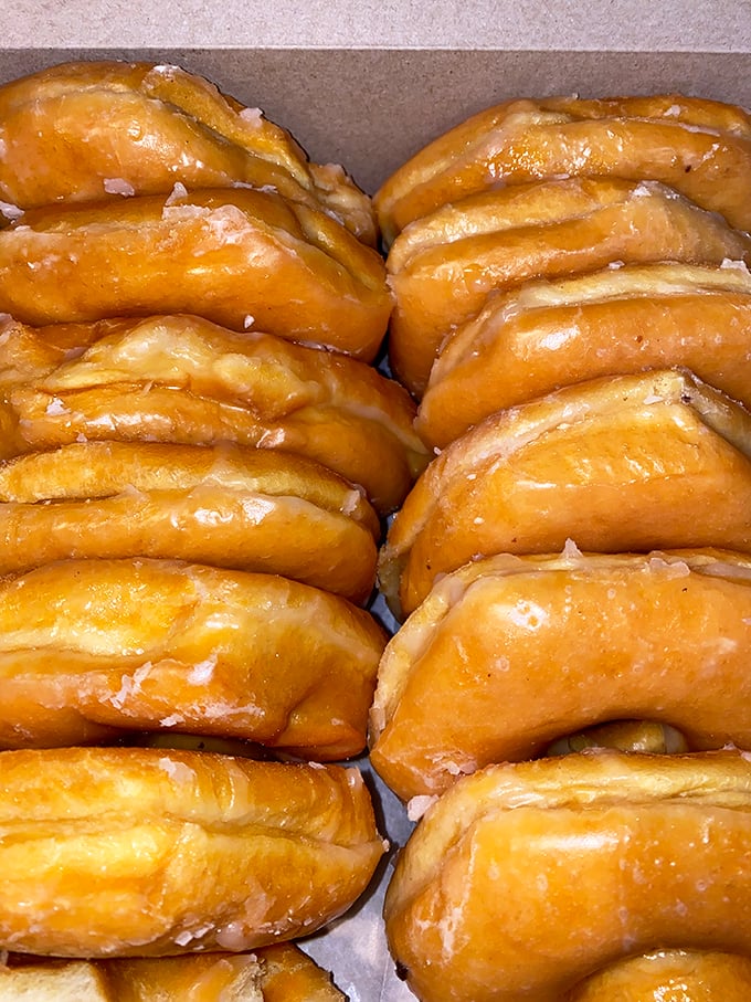 Rows of glazed donuts lined up like edible dominos, their honey-colored surfaces catching the light like amber in the morning sun.