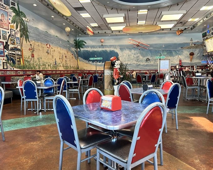 Red and blue chairs pop against beach murals, creating a dining space where every table feels like the best seat in the house.