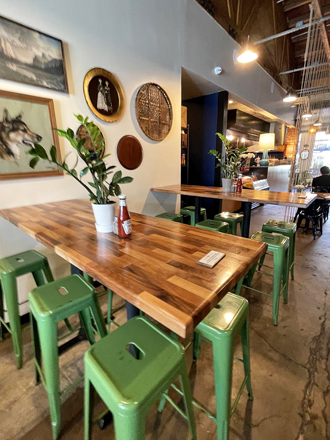 Green metal stools pop against butcher block tables while eclectic wall art creates a space that's equal parts gallery and cozy breakfast nook.