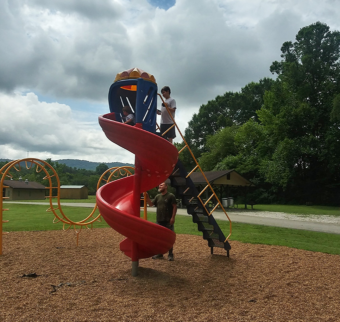 The playground's spiral slide stands like a castle tower, where kids rule kingdoms of imagination against a backdrop of mountains.