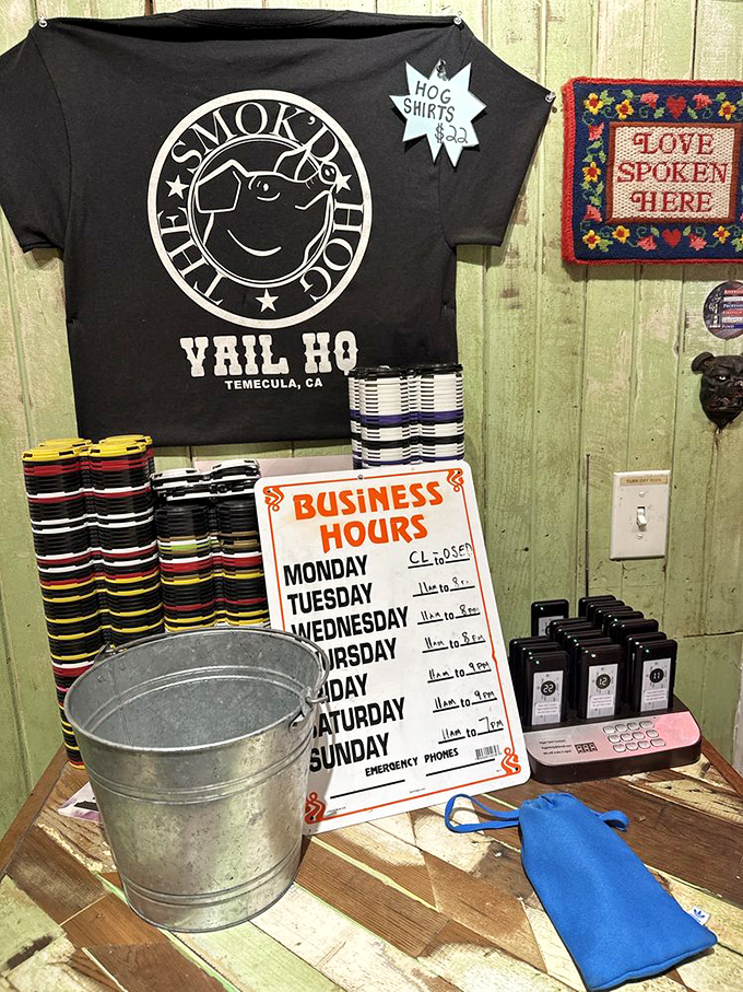 The wall says "Hog Shirts $22" but the needlepoint reminds us "Love Spoken Here." Both statements equally true in barbecue country.