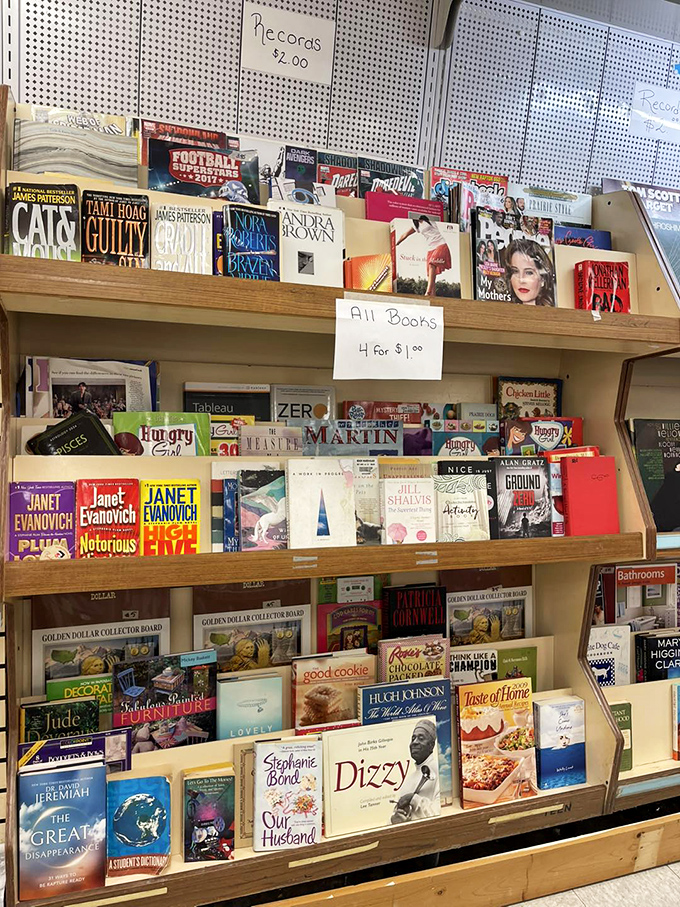 Literary treasures at four for a dollar – Janet Evanovich mysteries stacked alongside cookbooks and biographies. Bibliophile heaven at bargain prices.