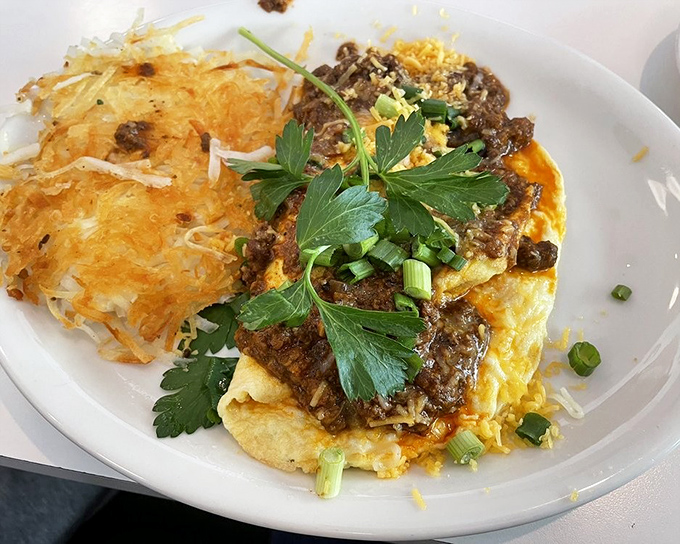 An omelet smothered in chili, topped with fresh herbs and paired with crispy hash browns—breakfast with a spicy personality.