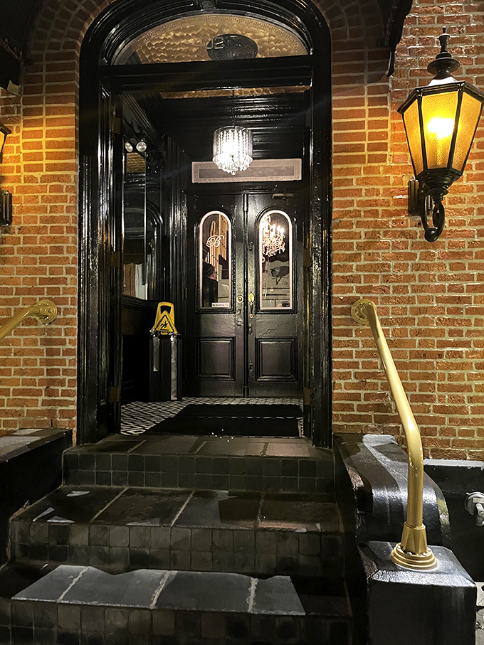 The entrance feels like a portal to another era. Those glossy black doors and warm brick promise an evening of Victorian splendor within.